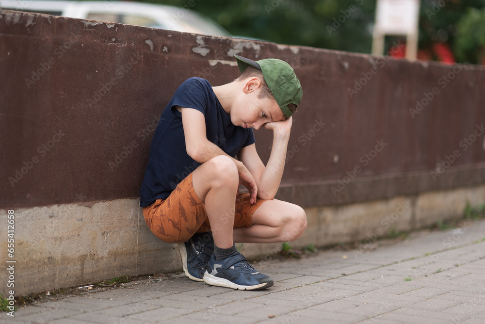 A teenage boy is squatting leaning against a concrete wall on the ...