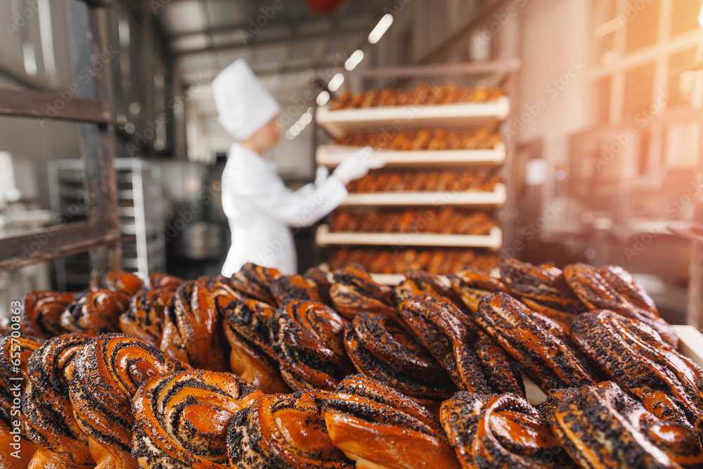 Worker woman baker in chef uniform hold buns with poppy seeds ...