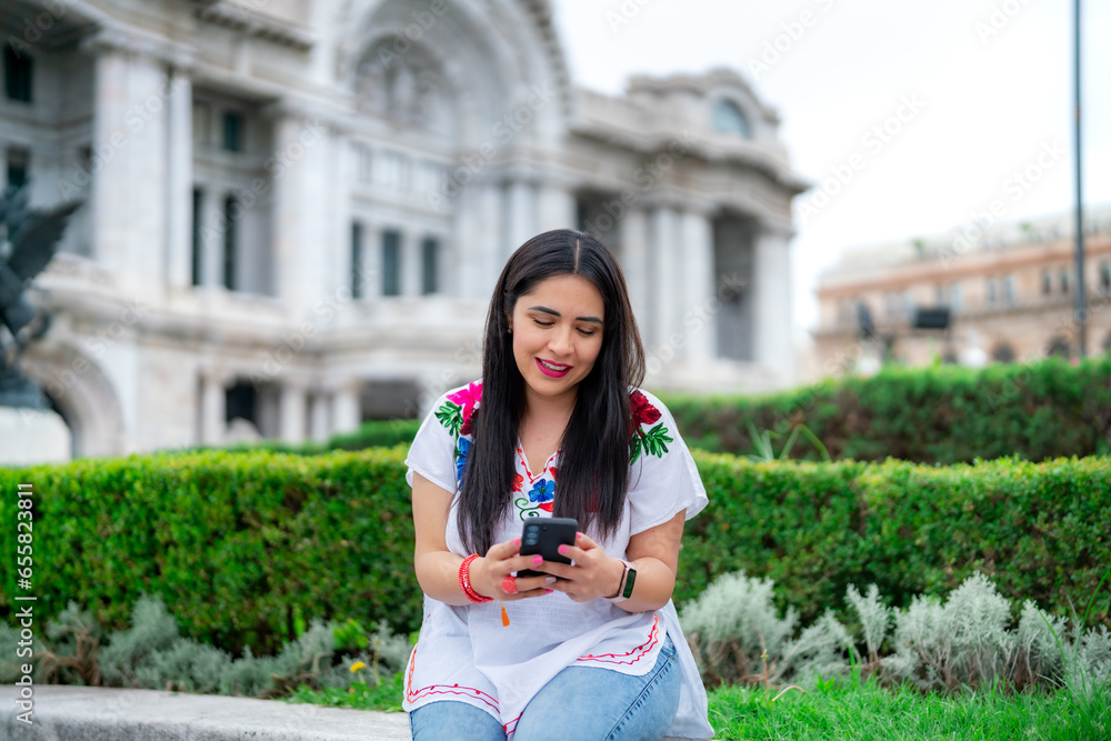 Happy young ethnic mexican woman using smartphone and looking at screen ...