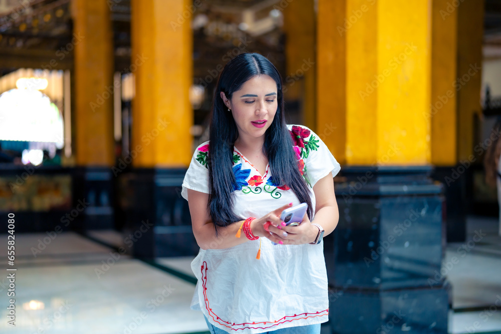 Happy young mexican woman tourist in embroidered top looking at screen ...