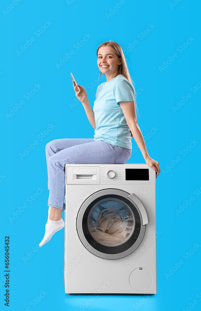 Pretty young woman sitting on washing machine and using mobile phone ...