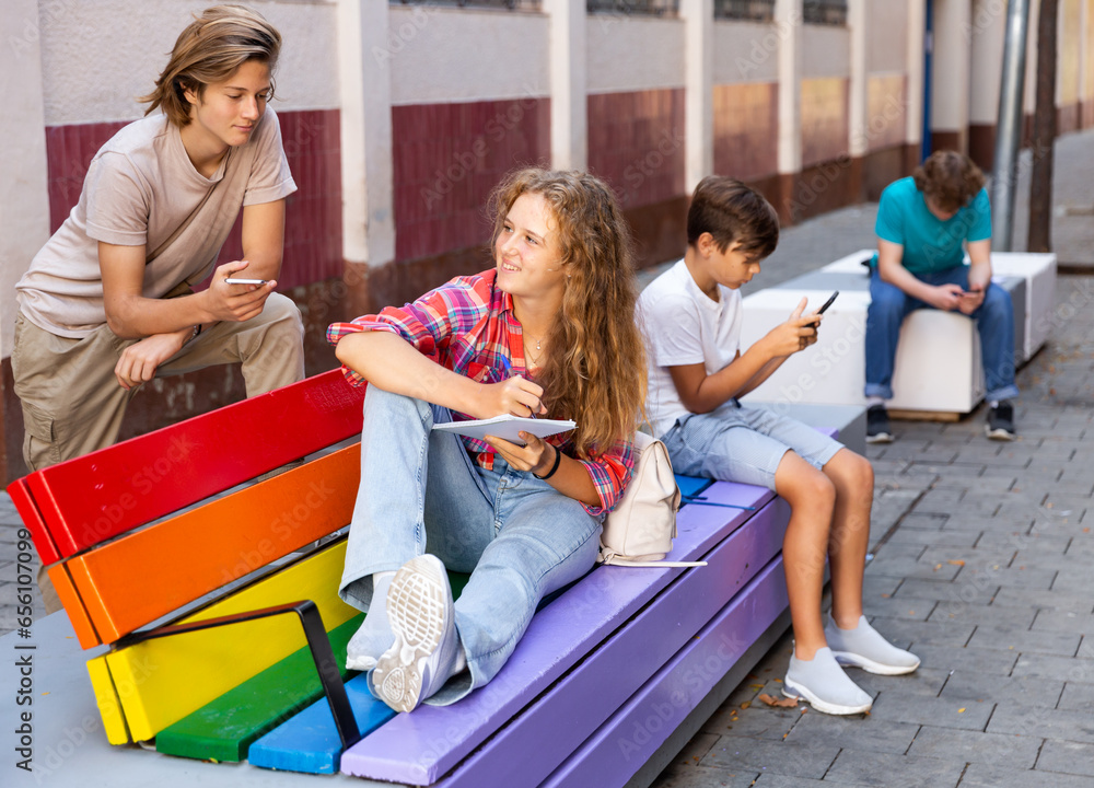 Teenager girl and young boy sitting on bench. Girl doing homework and ...