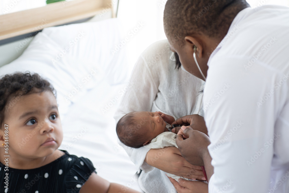 African pediatrician doctor doing check up newborn baby in mother's arm ...