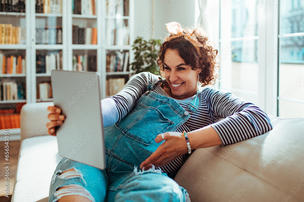 Young pregnant woman showing her bump on the video chat on a tablet at ...