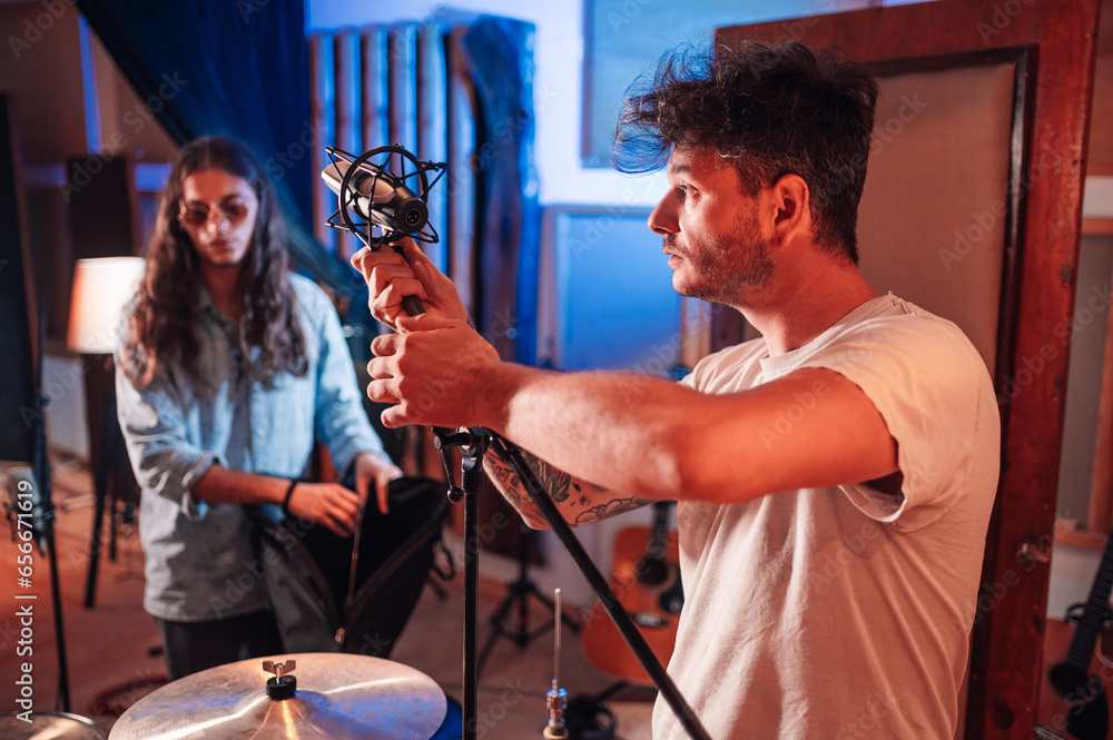 Sound technician setting up a condenser studio microphone above a drum ...