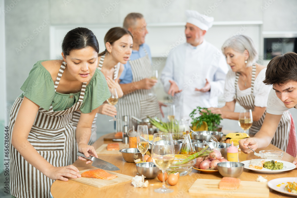 Interested young Asian woman in apron standing at table with groceries ...