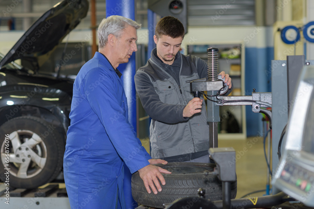 apprentice mechanic and teacher retreading wheel in automotive workshop ...