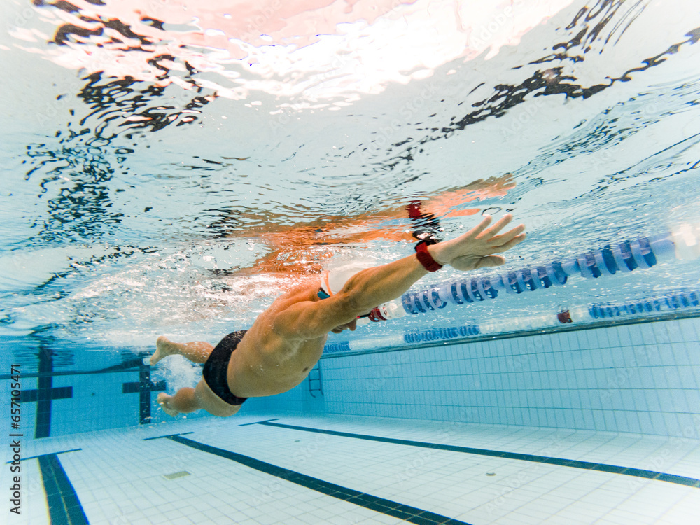 An adult man with an amputated arm is swimming underwater in a pool ...