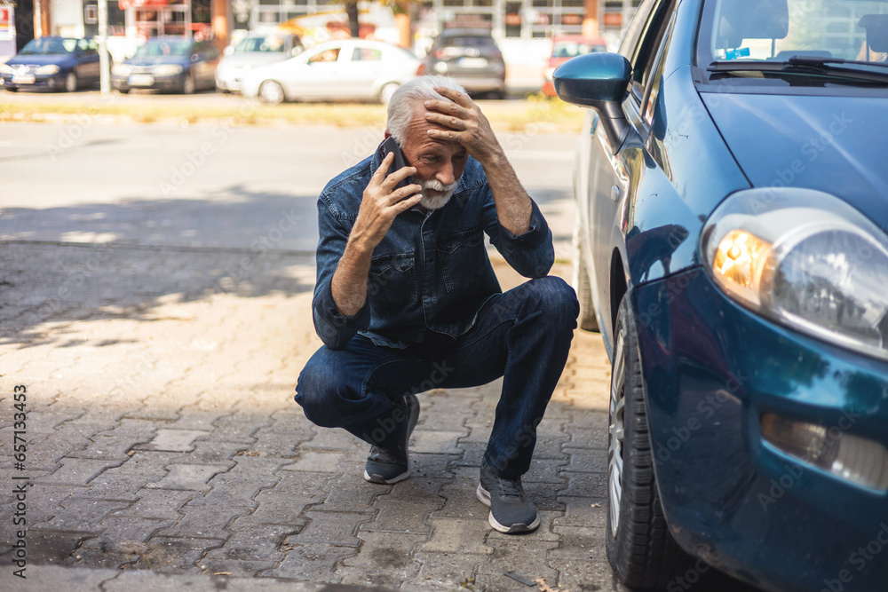 Portrait of a despair man crouching next to his car with flat tire ...