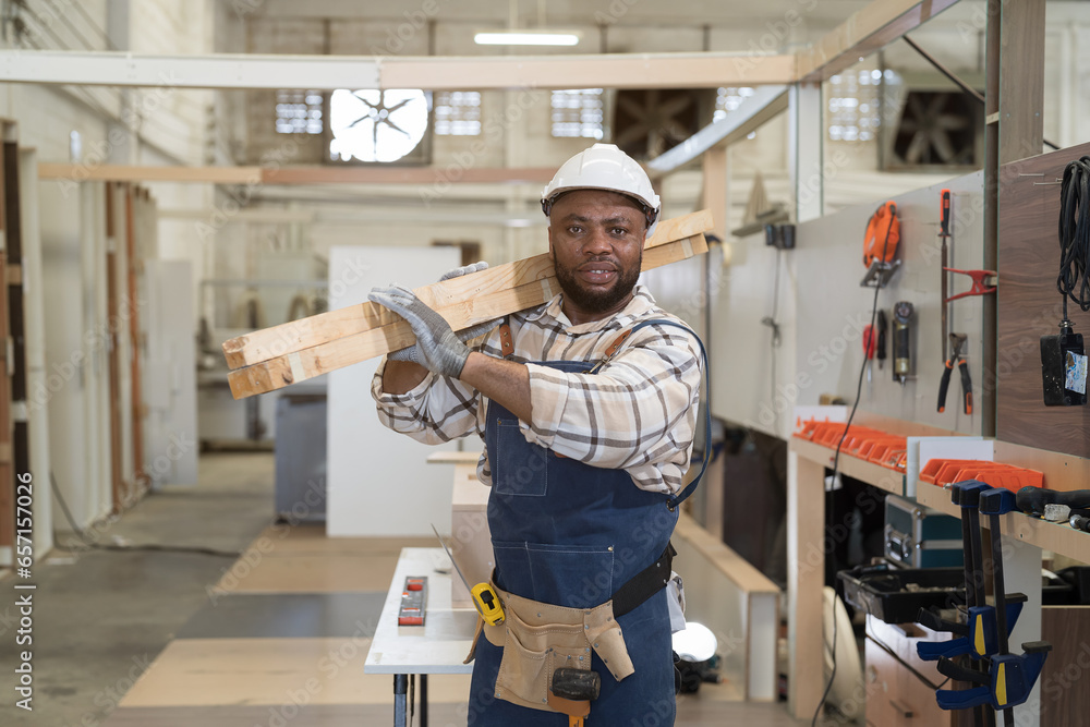 Male carpenter carrying piece of wood on his shoulder at wood ...