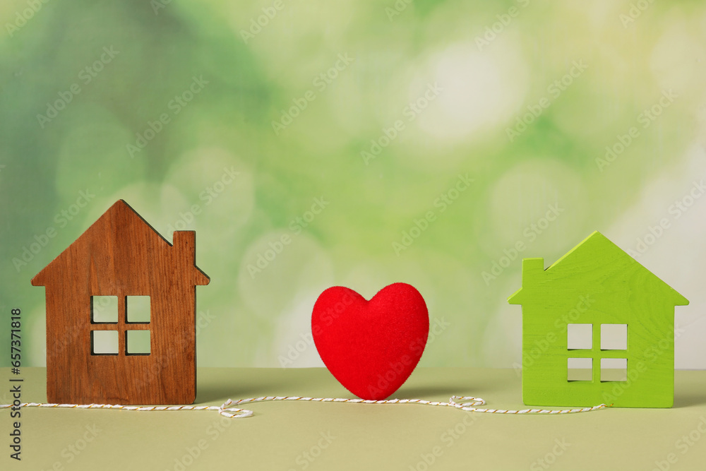 Red heart and decorative cord between two house models on light green ...