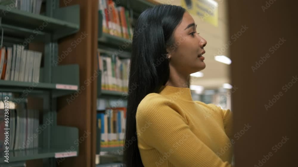 Pretty girl chooses books, standing in public library. Asian female ...