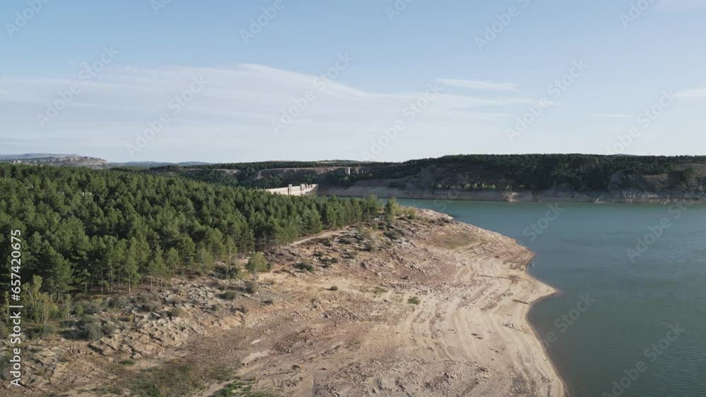 Dynamic linear aerial shot of a reservoir among pine trees with a low ...