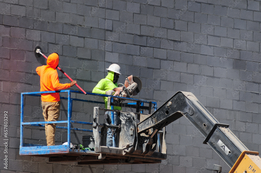Two construction workers on a telescopic boom lift, working on a tall ...
