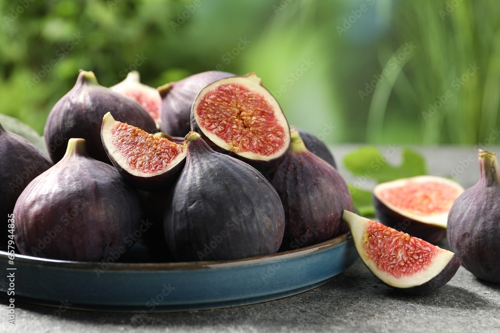 Whole and cut ripe figs on light grey textured table against blurred ...