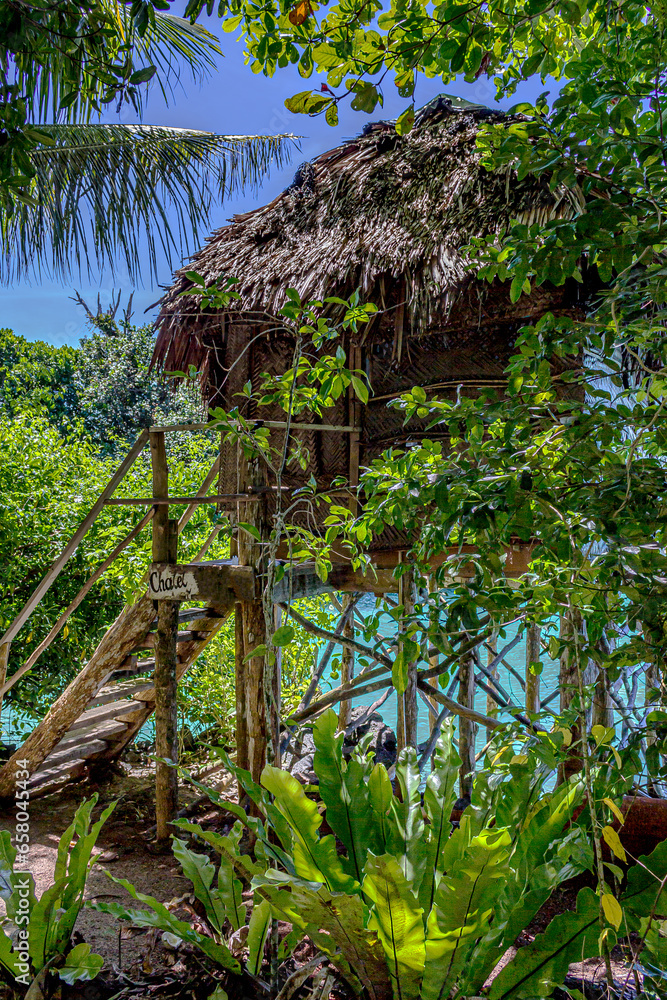 Wooden fale or house or hut with a thatched roof on stilts over the ...
