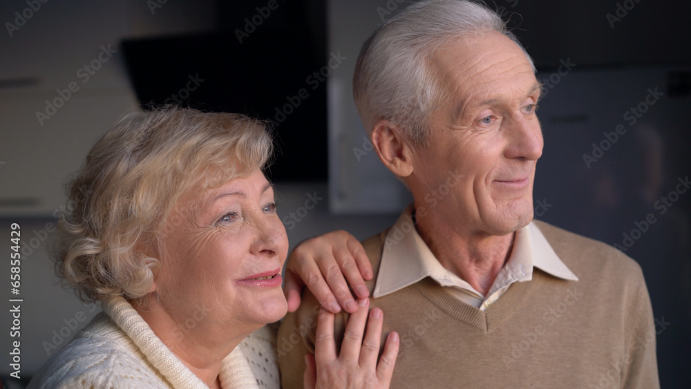 Nostalgic elderly couple smiling and hugging at home, reminiscing about ...