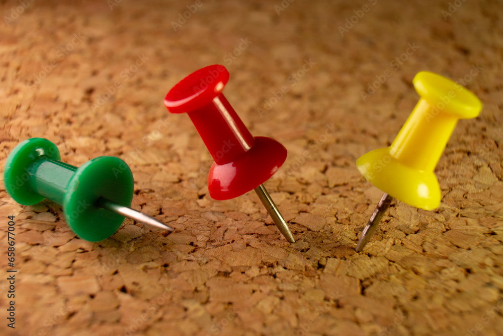 group of red, green and yellow pins seen in macro stuck on a cork board ...