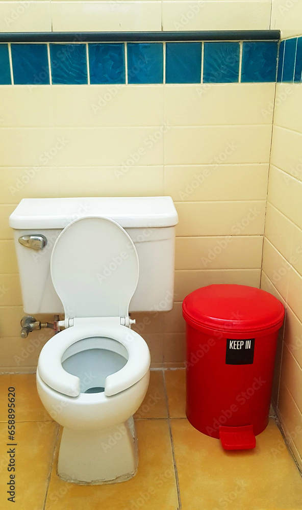 Flush toilet with red trash can on yellow tile in bathroom, restroom ...