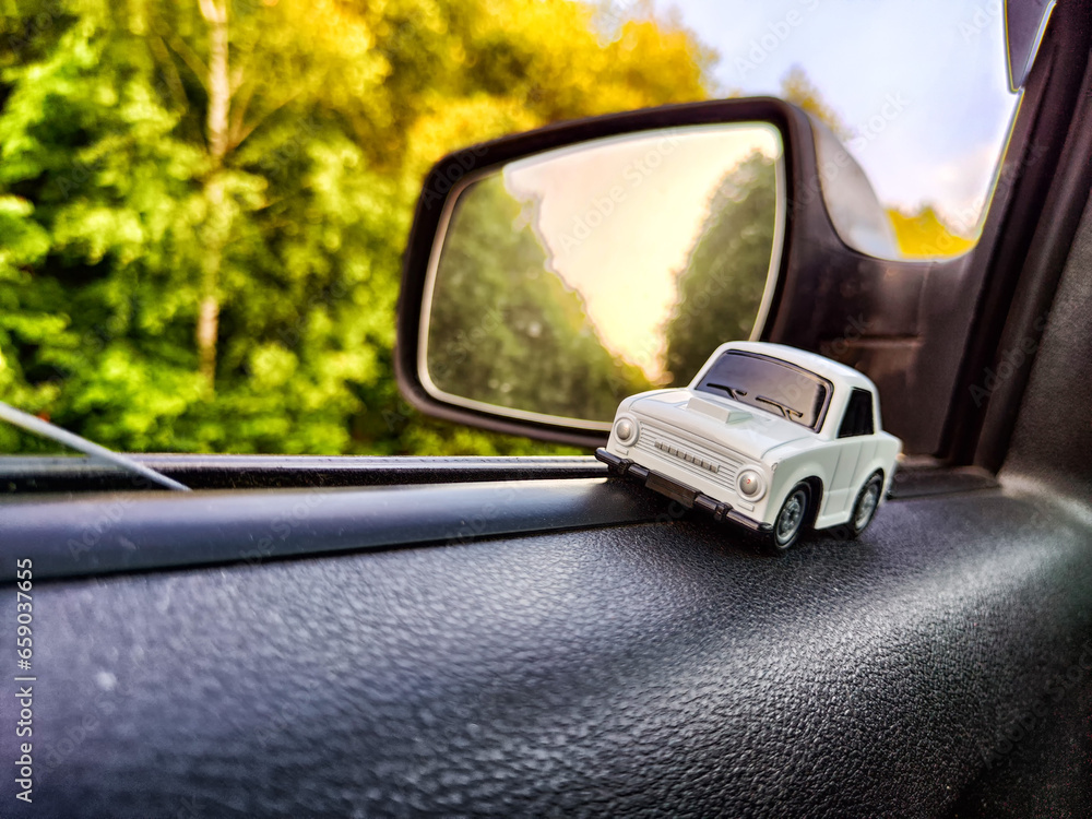 Small white toy car on background of side mirror of a real big caron ...