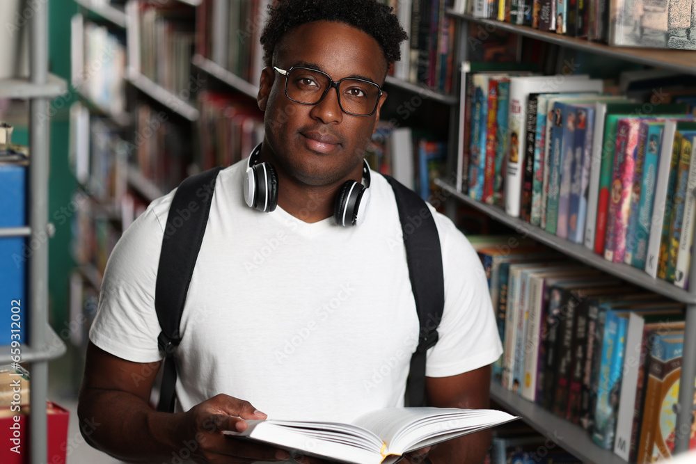 Smart handsome young man standing next to bookshelf, holding and ...