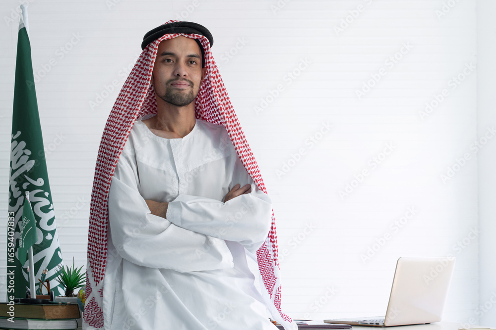 Arab Muslim man leans against his desk with his arms crossed over his ...