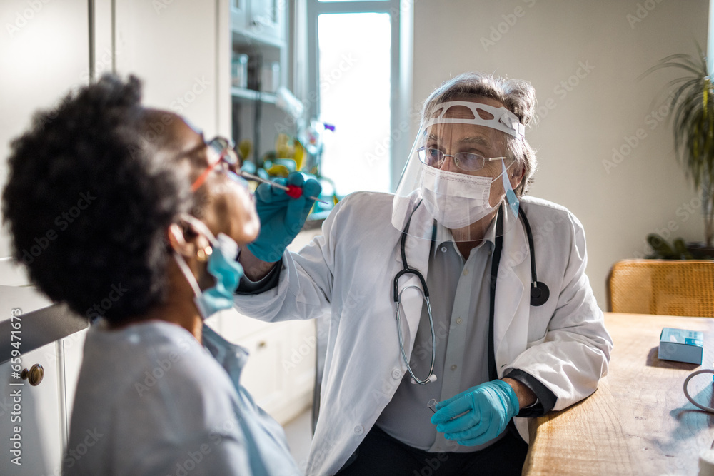 Senior home doctor performing a COVID-19 PCR test on a female patient ...