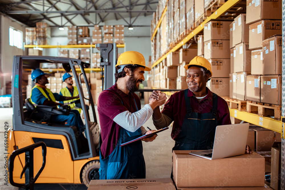Two diverse workers shaking hands while working in a warehouse together ...