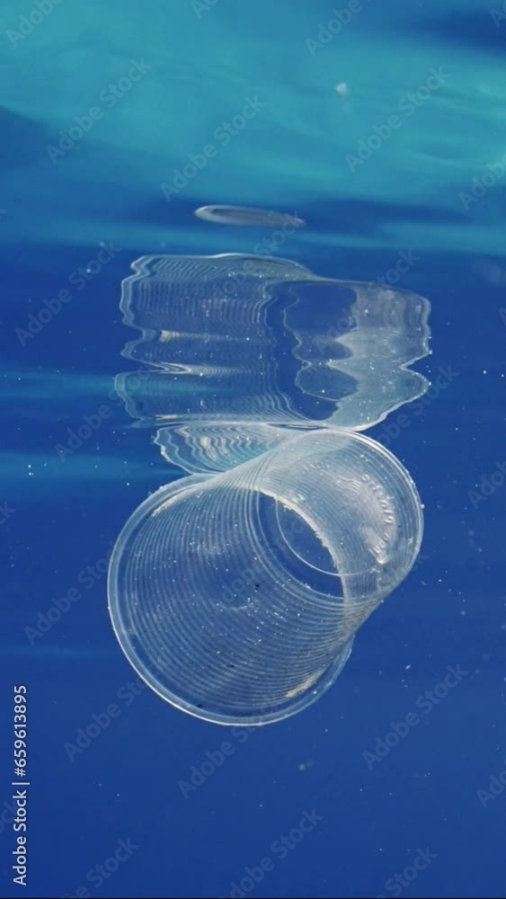 Vertical video, Close-up of plastic cup slowly floating under water ...