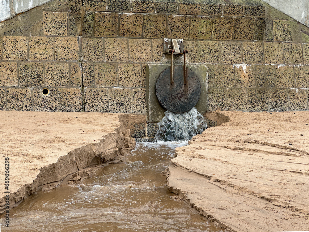 Basalt seawall promenade with rust steel waste gates, sewage pipes ...