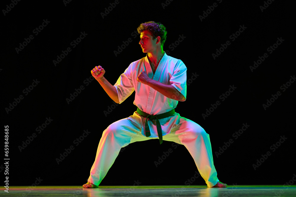Defense pose. Young guy in white kimono practicing over black studio ...