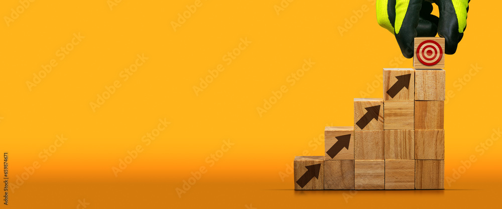 Gloved hand arranging wood blocks as step stair with a target symbol on ...