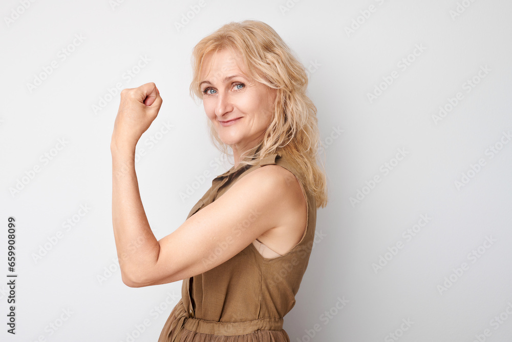Portrait of confident 50 year old woman showing biceps, demonstrating ...