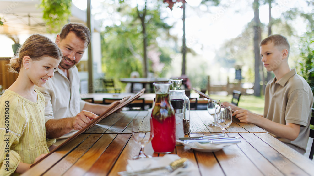 Father and kids reading menus in a restaurant, choosing food and drinks ...