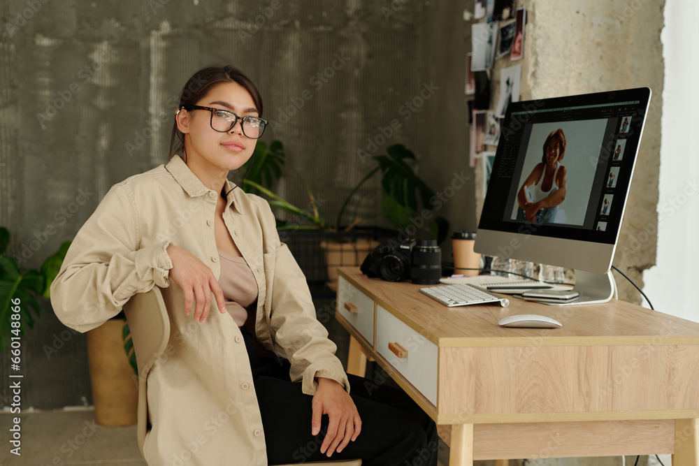 Brunette female photographer sitting by desk with computer monitor with ...