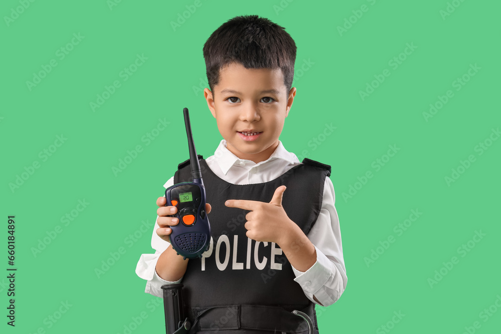 Cute little police officer pointing at radio transmitter on green ...