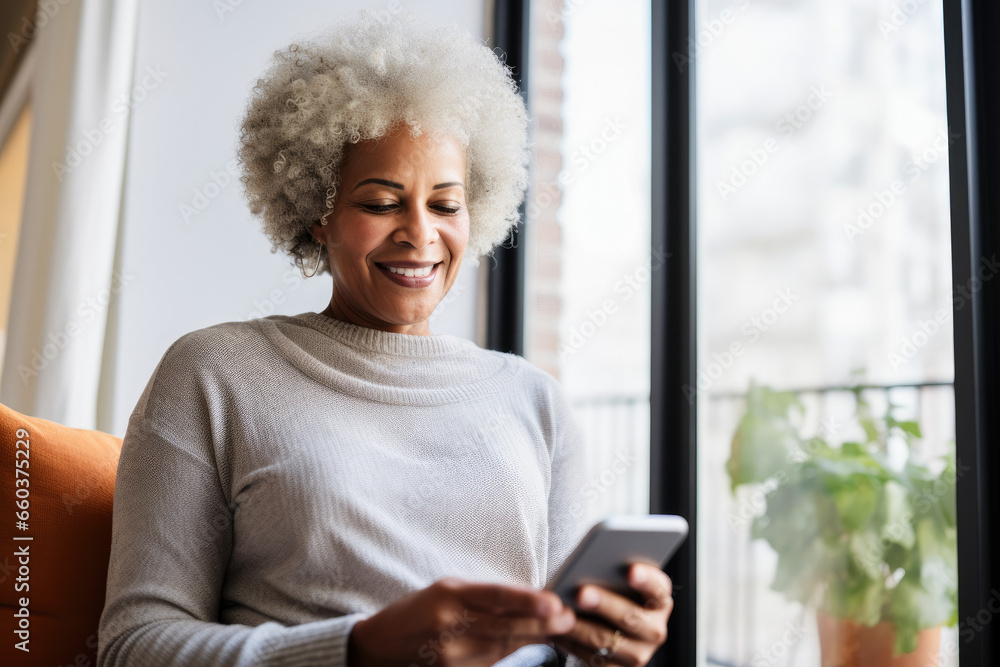 Portrait of a relaxed senior woman laughing while using her smartphone at home. Modern lifestyle ...
