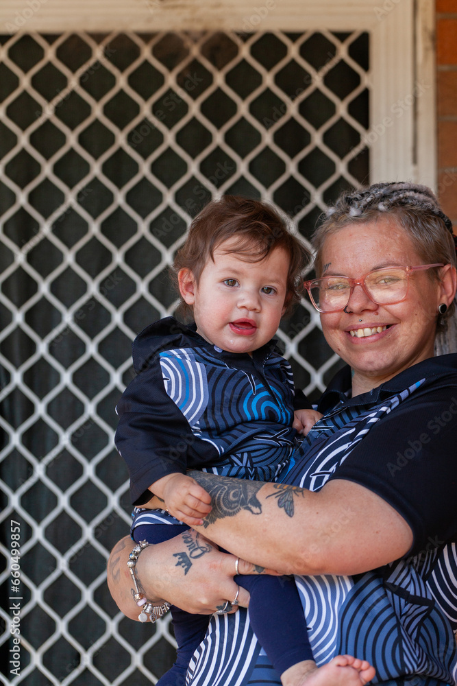 Smiling portrait of First Nations Australian mum with baby girl by door ...