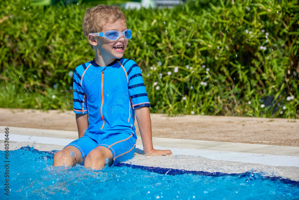 Satisfied boy in a blue bathing suit smiles, sits near the pool ...