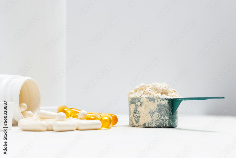 Whey protein powder in measuring spoon, white capsules of amino acids ...