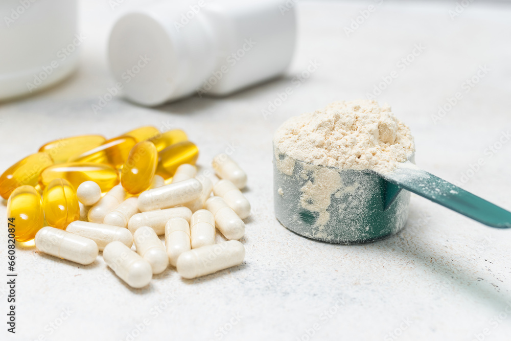 Whey protein powder in measuring spoon, white capsules of amino acids ...