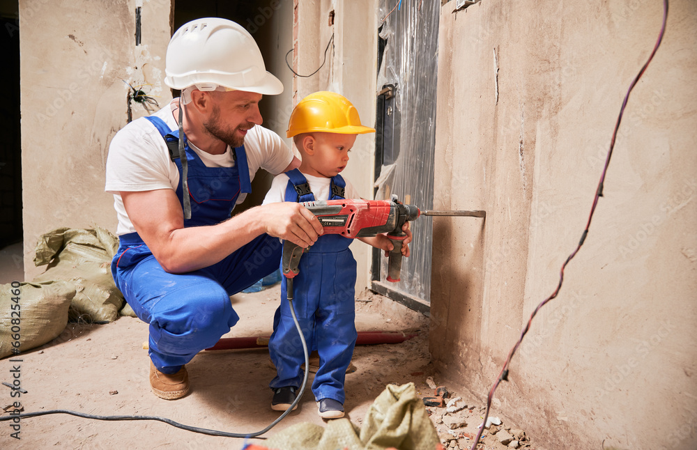 Man and little boy construction workers drilling wall with electric ...