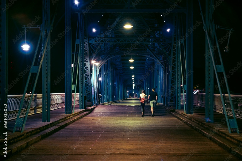 two people walking across a bridge at night, the people are walking ...