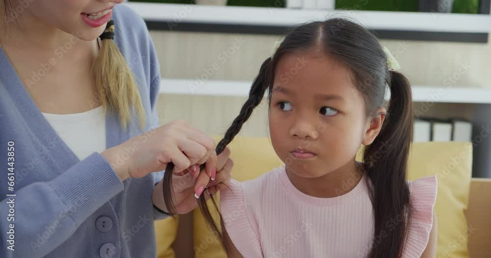 Caring mother braiding pigtail to asian little daughter. Mother braids ...