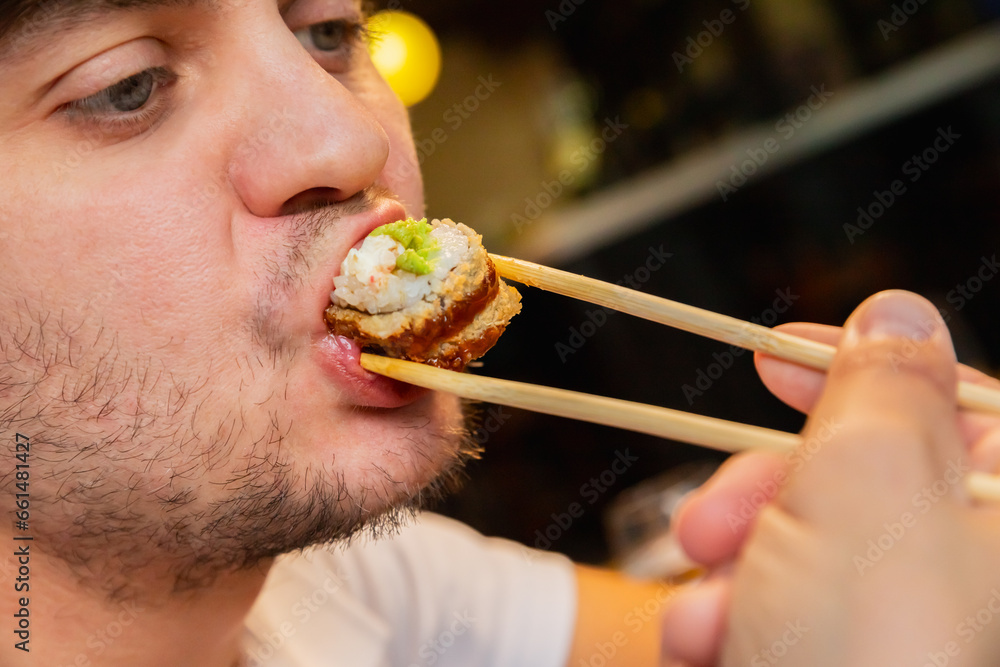 Young adult male man eating baked Japanese sushi roll with bamboo ...