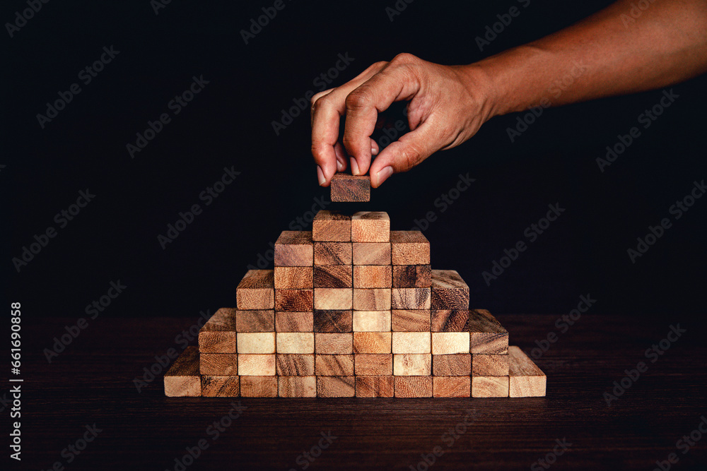 Hand placing wooden block tower stack in pyramid stair step with ...