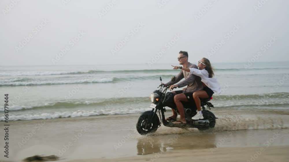 Young couple ride motorcycle, splashing water on wet sandy sea beach in ...