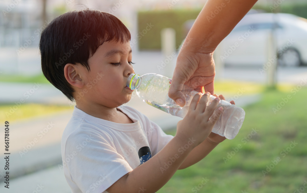 Mother giving a bottle of clean water to her son and help him to ...