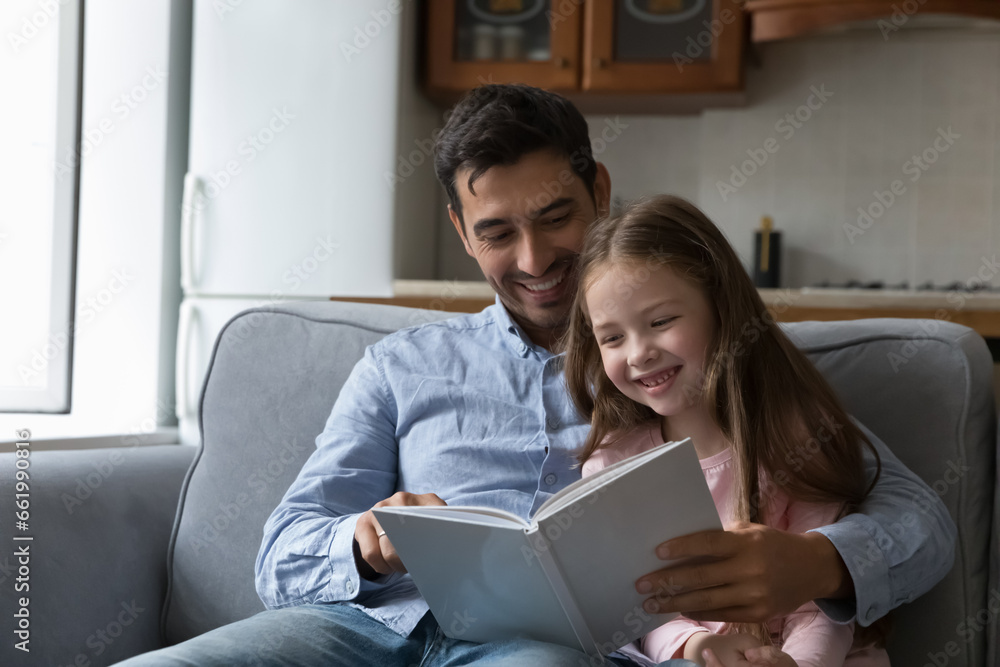 Happy joyful dad teaching cute little daughter to read, hugging kid ...