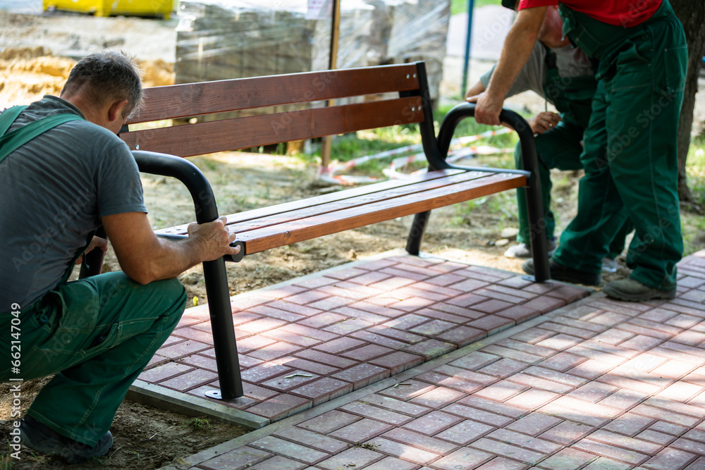 Physical workers set up a park bench at a designated spot in a city ...